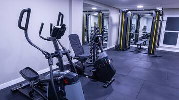 Uma academia com equipamentos de ginástica, um espelho e uma porta que dá para outro espaço.