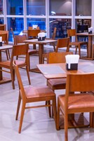 Restaurante com mesas e cadeiras de madeira, porta-guardanapos preto e vista através de grandes janelas.
