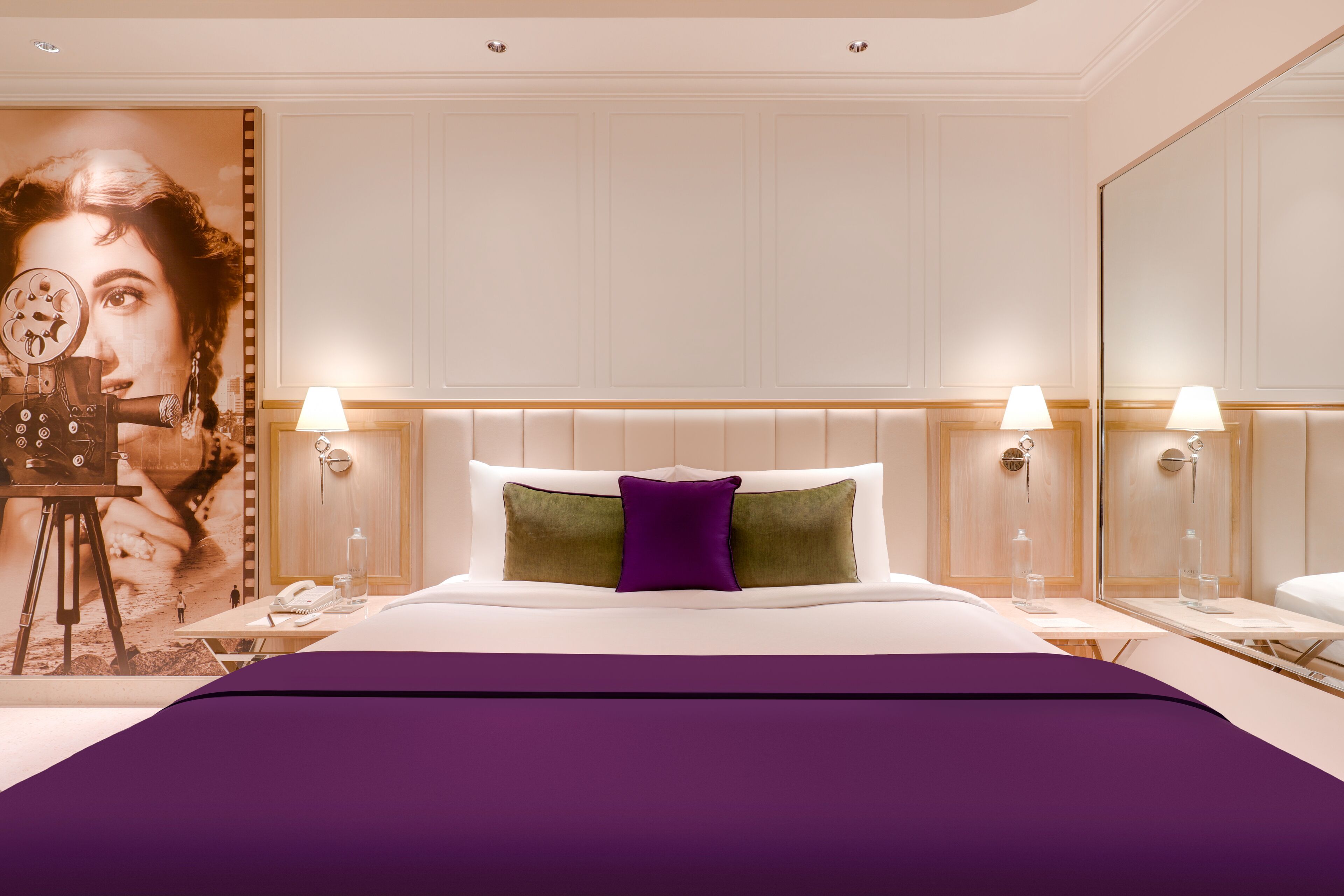 Quarto de hotel com uma cama grande, duas mesas de cabeceira, um espelho e uma luminária fixada na parede.