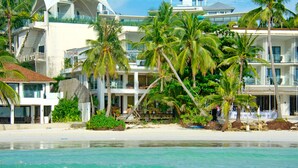 Um hotel à beira-mar com várias varandas, palmeiras e uma praia de areia.
