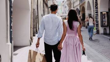 Um casal caminhando por uma rua de paralelepípedos, de mãos dadas e carregando sacolas de compras.