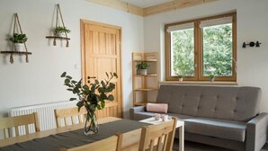 Uma sala de estar aconchegante com uma mesa de jantar de madeira, um sofá cinza e uma janela com vista para o verde.