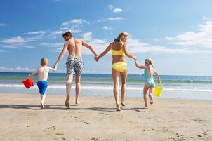 Uma família caminhando numa praia de areia, com o oceano ao fundo.