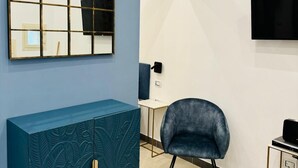 Quarto moderno com parede azul, um armário com espelho, uma cadeira azul escura, uma mesa pequena e uma TV fixada na parede.