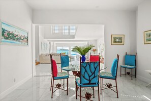 Uma área de refeições com mesa de vidro e cadeiras, um vaso com plantas e obras de arte nas paredes.