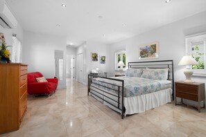 Quarto com cama, um sofá vermelho, cómoda de madeira e janela com persianas.