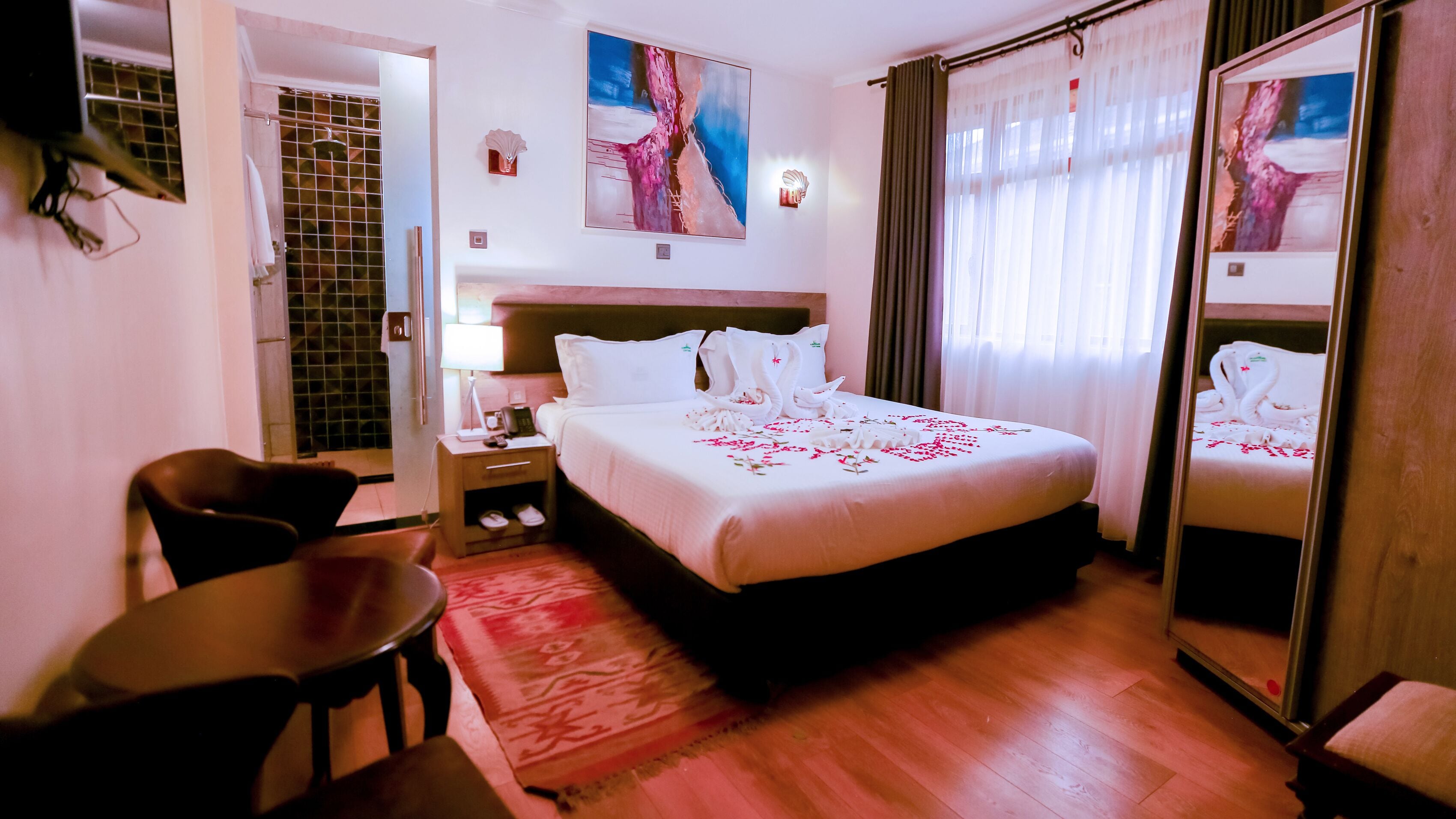 Quarto de hotel com cama, escrivaninha, cadeira, mesa de cabeceira e espelho.
