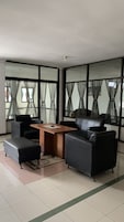 Uma sala de estar moderna com um sofá, duas poltronas, uma mesa de centro e grandes janelas com cortinas leves.