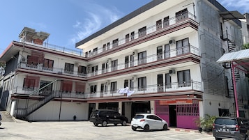 Um edifício de vários andares com varandas, uma escadaria e um estacionamento com carros.