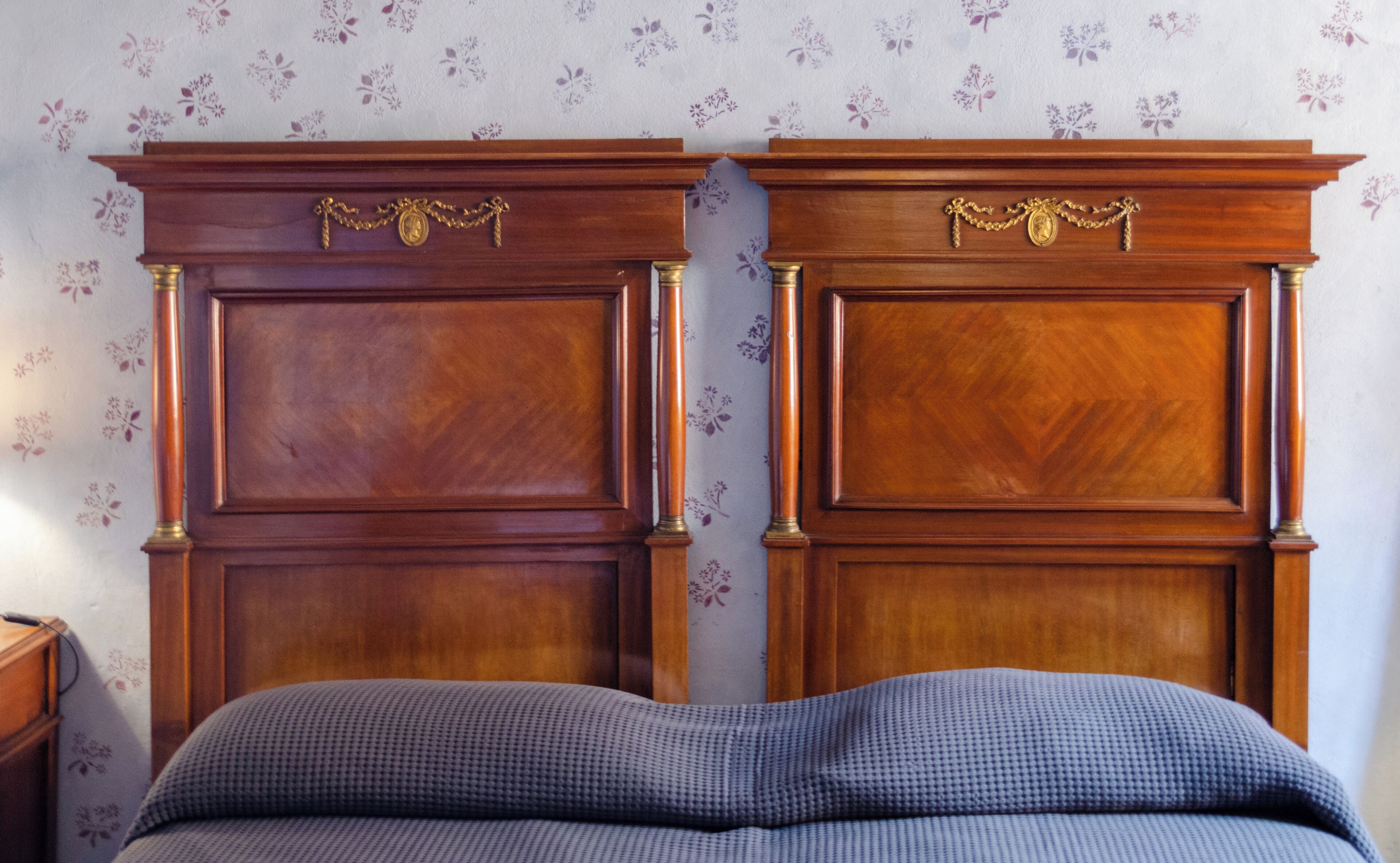 Quarto com uma cama de casal, cabeceira de madeira com detalhes dourados e papel de parede floral.