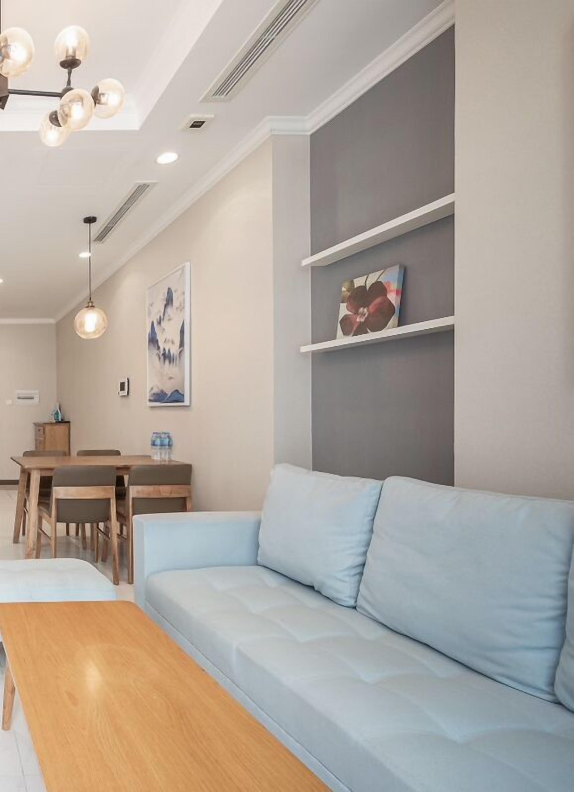 Uma sala de estar moderna com um sofá azul claro, mesa de jantar de madeira e luminária no teto.