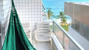 Uma varanda com rede, cadeiras brancas e vista para o mar.