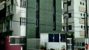 Um edifício residencial de vários andares com um núcleo central, varandas e entrada protegida por portão.