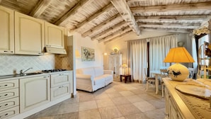 Uma cozinha espaçosa com armários brancos, uma sala de jantar com mesa e cadeiras, e uma sala de estar com sofá e luminária.