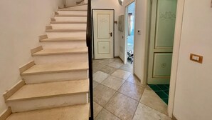 Escadaria que leva a um patamar com uma porta, piso de azulejos e um interruptor na parede.