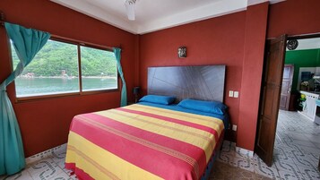 Quarto com cama, cortinas, vista para um lago e porta que dá para uma cozinha.