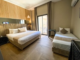 Quarto de hotel com duas camas, cabeceira de madeira, uma mesa pequena e varanda com vista.