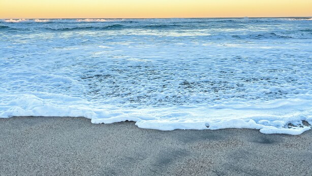 Uma praia com ondas suaves beijando a costa sob um céu claro.