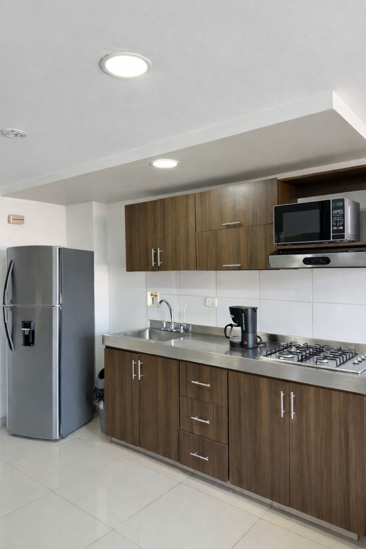 Cozinha moderna com eletrodomésticos de aço inoxidável, armários de madeira e painel de azulejos.