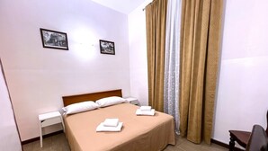 Quarto de hotel com cama, duas mesas de cabeceira, uma cadeira e duas fotografias emolduradas na parede.