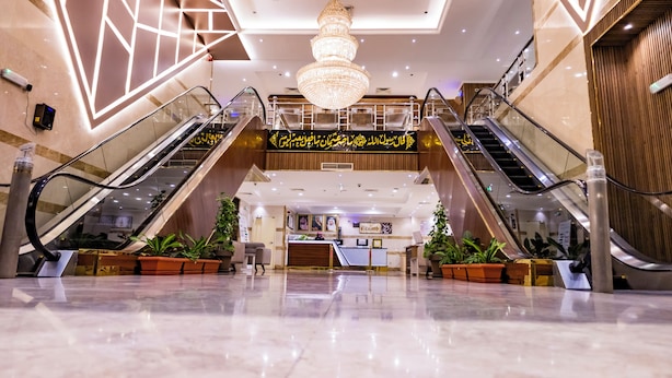 Um hall de hotel com um lustre, escadas rolantes, plantas em vasos e um balcão de recepção.