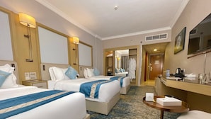 Quarto de hotel com duas camas, uma escrivaninha, uma cadeira, uma mesinha e um banheiro visível por uma porta aberta.