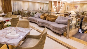 Um lobby moderno de hotel com uma receção de mármore, assentos confortáveis, uma escadaria e um candelabro.