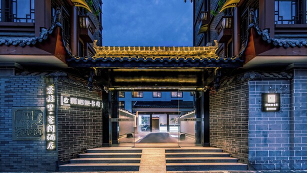 Um portão tradicional chinês com entrada moderna, paredes de tijolo e um caminho bem definido para o interior.