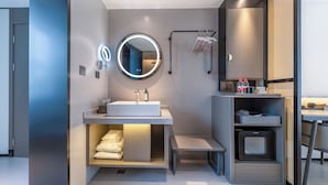Uma casa de banho moderna com lavatório embutido, um espelho redondo com iluminação integrada, um porta-toalhas e uma pequena estante com artigos de higiene pessoal.