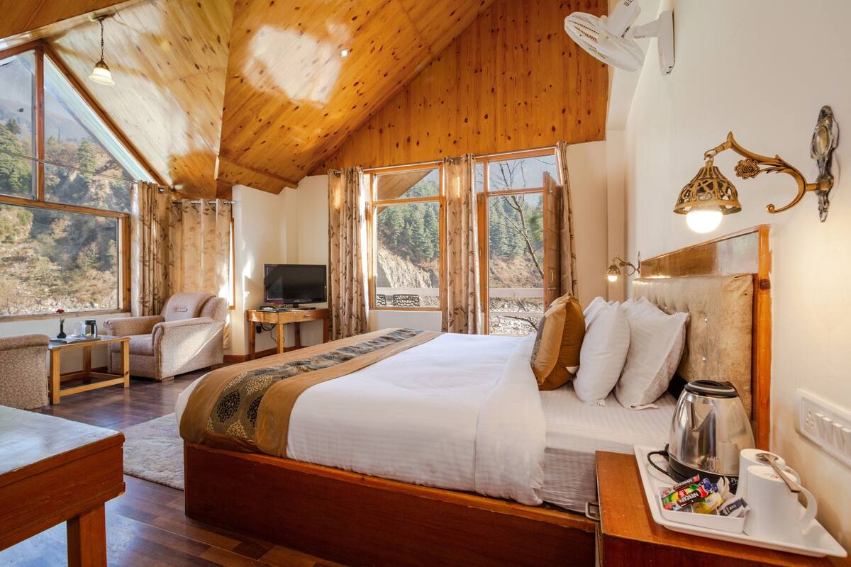 Quarto de cabana de madeira com uma cama, uma TV, uma cadeira e uma mesa com chaleira e xícaras.