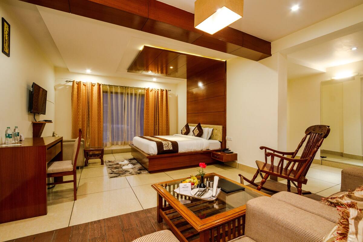 Quarto de hotel com cama, escrivaninha, cadeira, mesinha de centro e televisão.