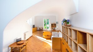 Uma sala de estar espaçosa, com teto alto, sofá, mesa de centro e estante de madeira.