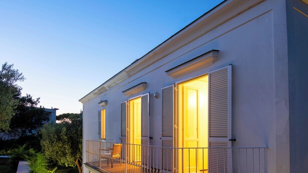 Uma casa de dois andares com varanda, um pátio com cadeiras e mesa, e um jardim.