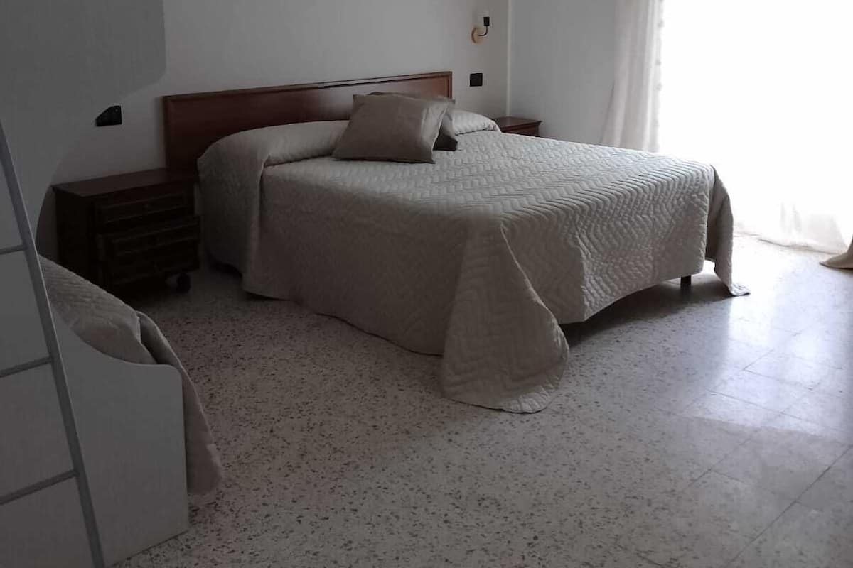 Um quarto com uma cama, uma mesa de cabeceira, um penteado e uma janela com cortinas.