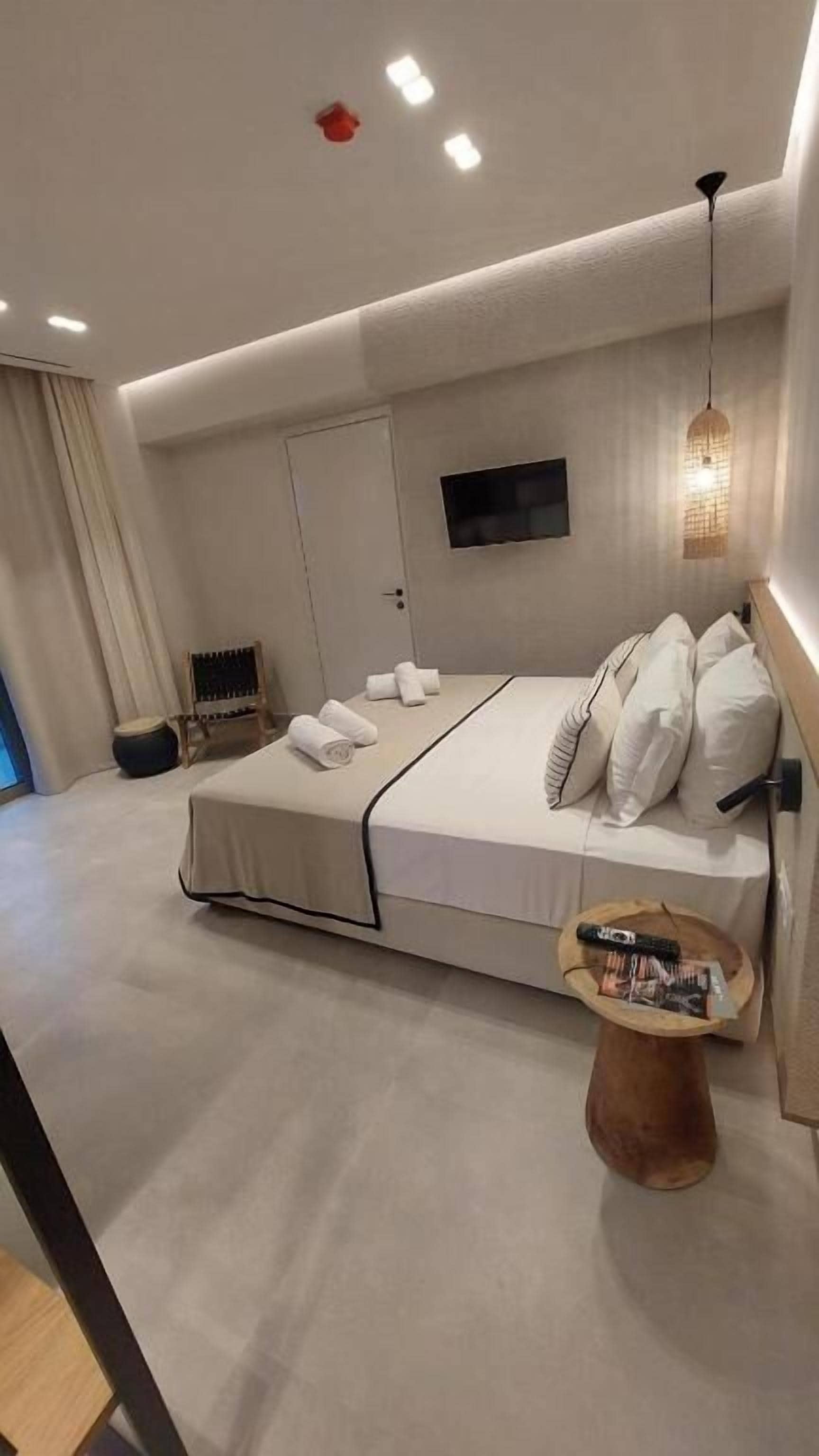 Quarto de hotel moderno com uma cama grande, uma TV de tela plana na parede e uma pequena mesa de madeira.