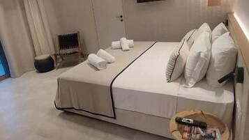 Quarto de hotel moderno com uma cama grande, uma TV de tela plana na parede e uma pequena mesa de madeira.