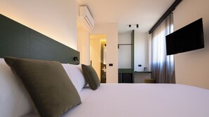 Quarto de hotel com uma cama grande, uma TV de tela plana na parede e um espaço separado para chuveiro e vaso sanitário.