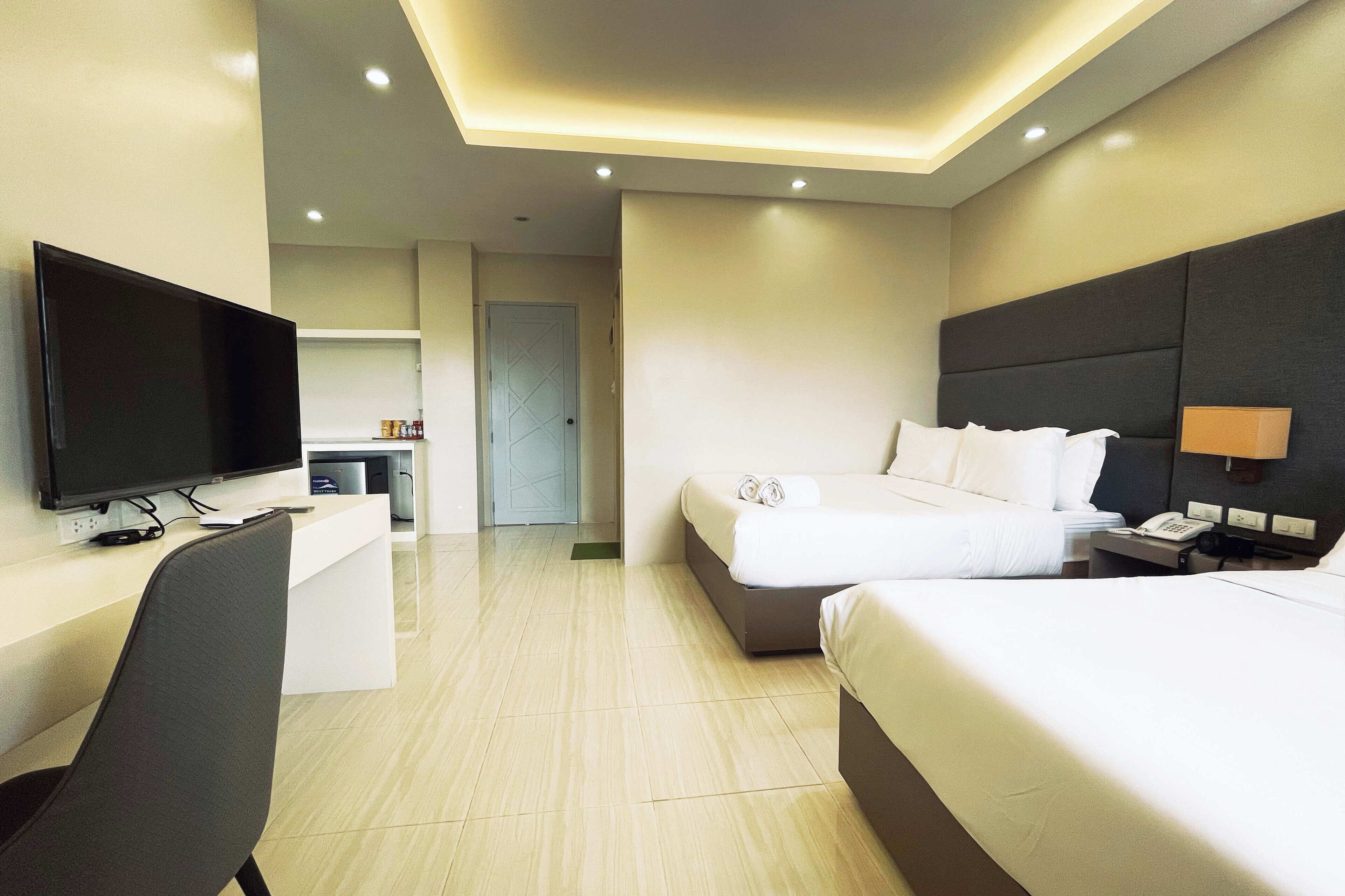 Quarto de hotel com duas camas, uma mesa de escritório, uma televisão de tela plana, uma cadeira e uma mesa de cabeceira com abajur.