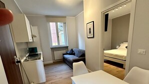 Um espaço compacto com cozinha compacta, área de refeições com mesa e cadeiras, sofá e cama em quarto separado.