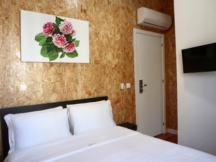 Quarto de hotel com uma cama, televisão na parede e uma porta.