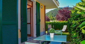 Um pátio externo com mesa e cadeiras, um vaso de planta e vista para uma encosta.
