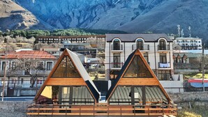 Um chalé de montanha com duas cabanas de madeira triangulares, um edifício principal com varandas, e montanhas nevadas ao fundo.