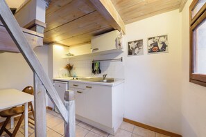 Cozinha com armários brancos, escada de madeira e janela.