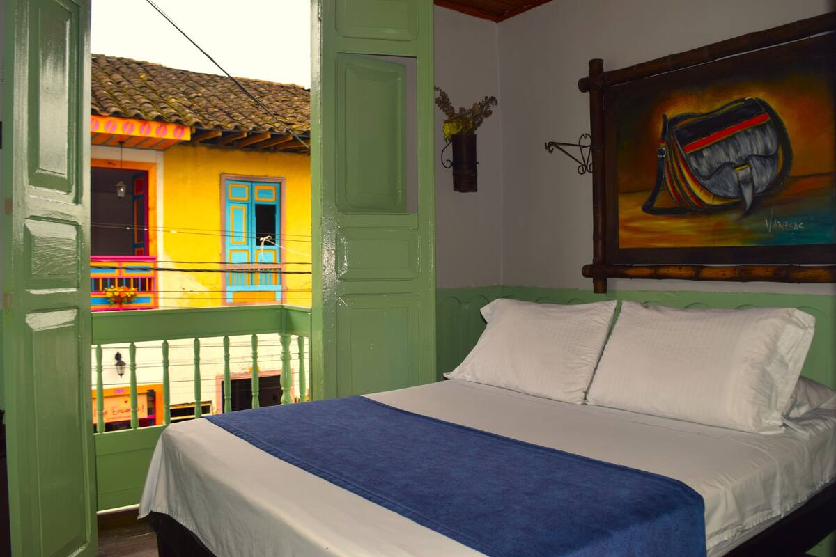 Um quarto com uma cama, uma porta verde, uma parede amarela e um quadro.