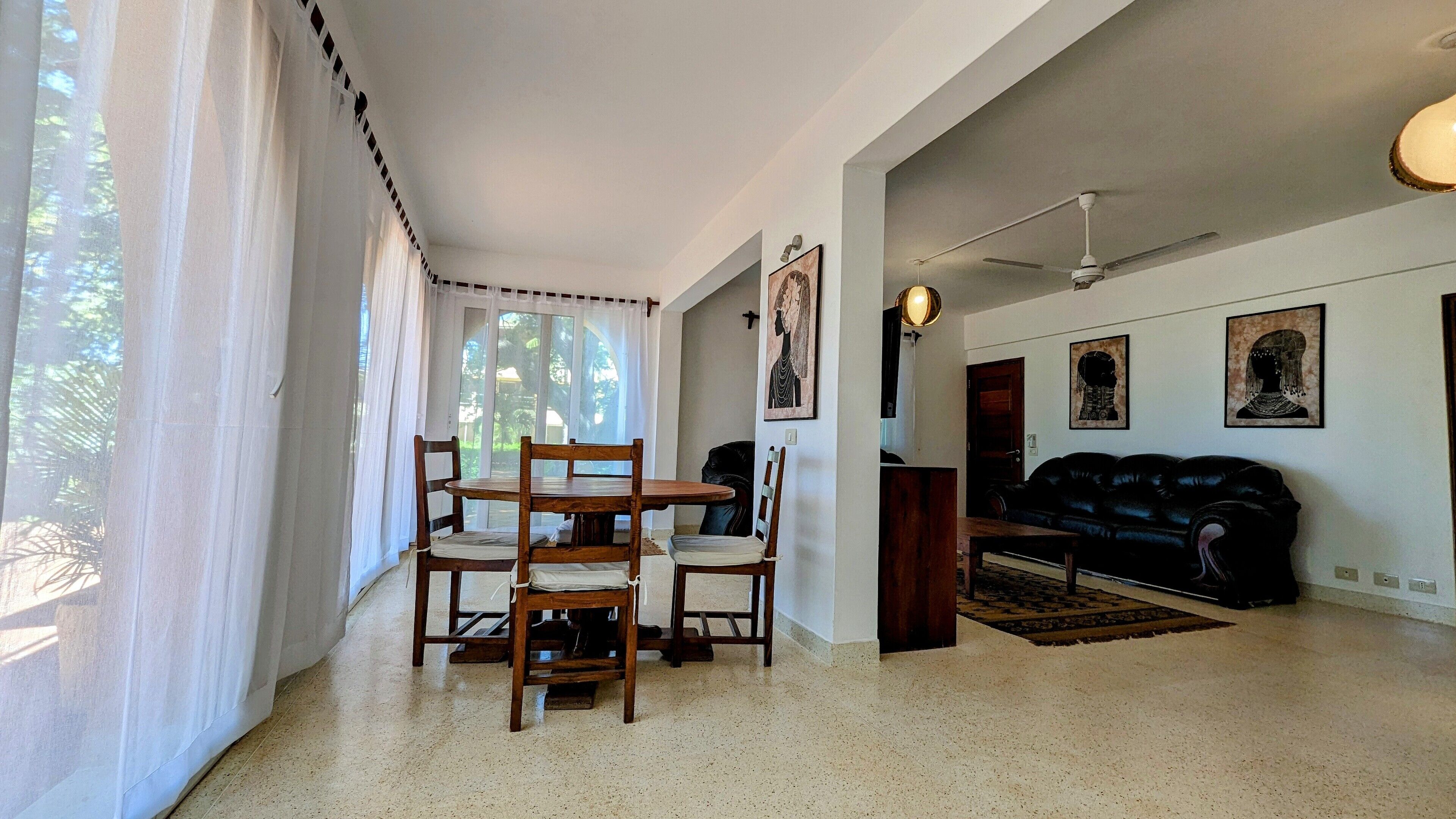 Uma sala de jantar com mesa e cadeiras, um sofá preto e obras de arte nas paredes.