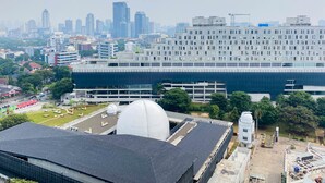 Um edifício moderno com telhado plano, janelas amplas e uma estrutura de cúpula central.