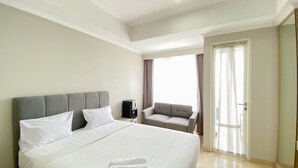 Quarto de hotel com uma cama grande, cabeceira cinza, um sofá e uma porta que dá para uma varanda.