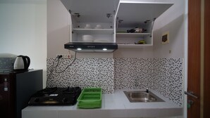 Uma cozinha com fogão a gás, pia, cesto verde e coifa sobre o fogão.