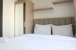 Uma cama bem arrumada com roupa de cama branca, uma cabeceira com design acolchoado e um guarda-roupa de madeira à esquerda.