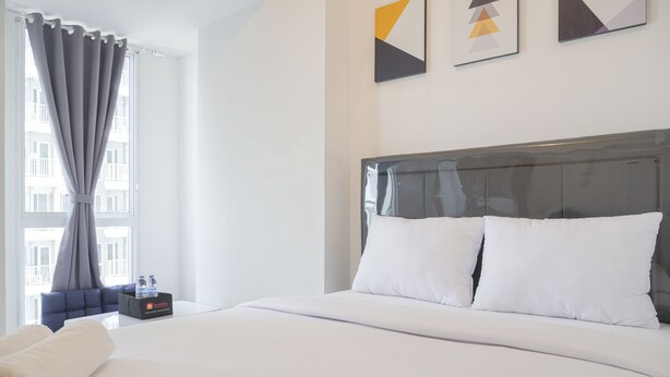 Quarto de hotel com cama grande, cabeceira, janela com cortinas, pequena mesa com uma garrafa e parede com arte geométrica.